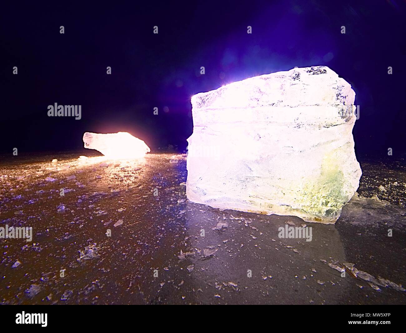 Blue ice cubes shine on flat glacier surface. Thanks to spot light ...