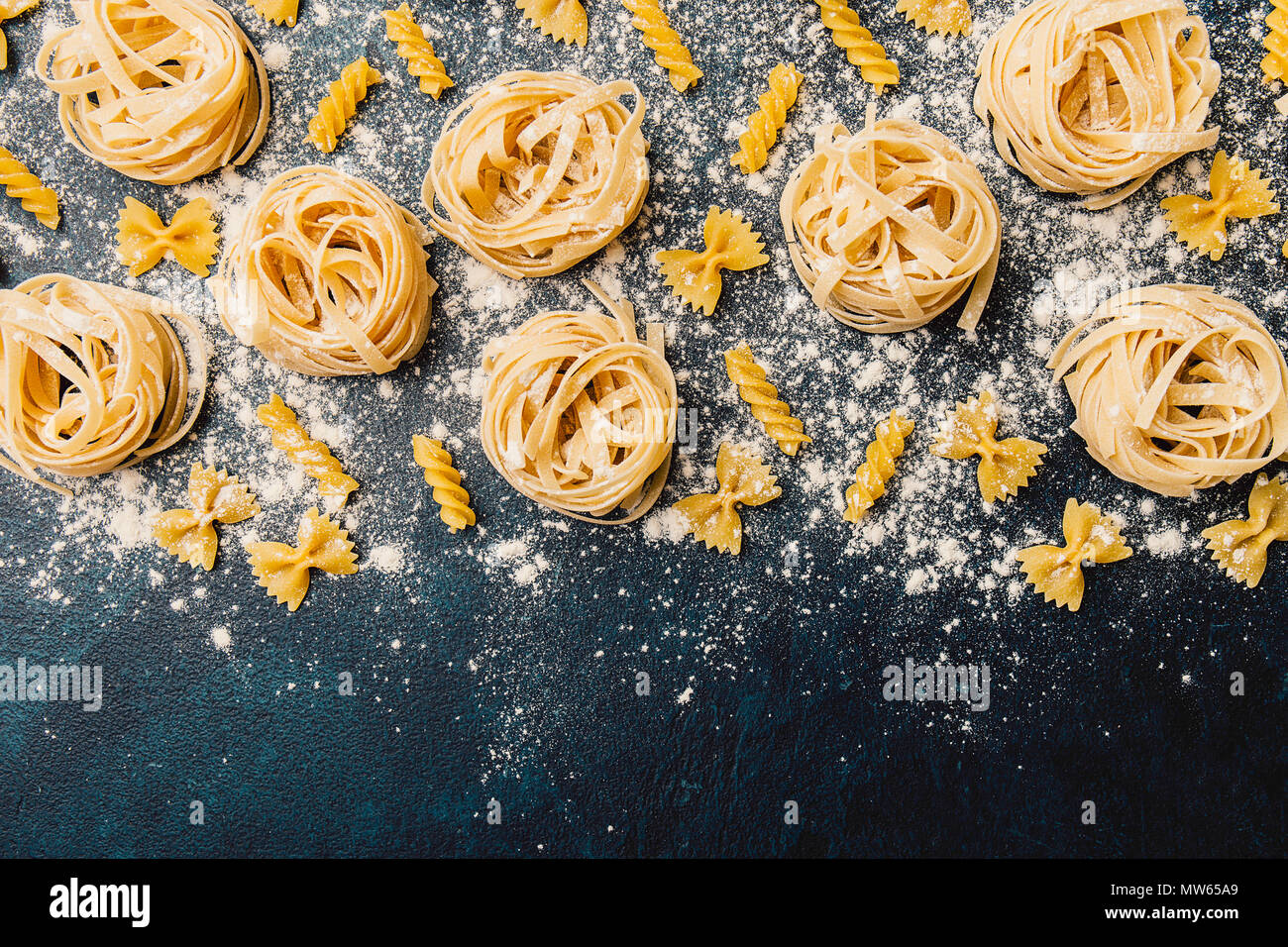 Various uncooked pasta scattered in flour on black background Stock ...