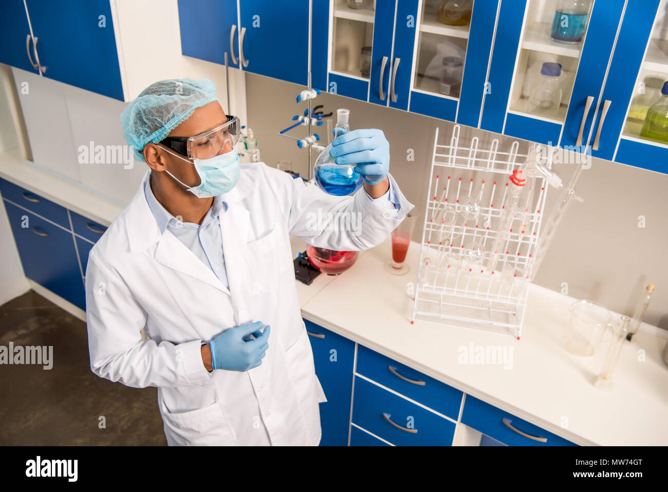 Scientist in protective gear examining test tube with blue liquid at ...