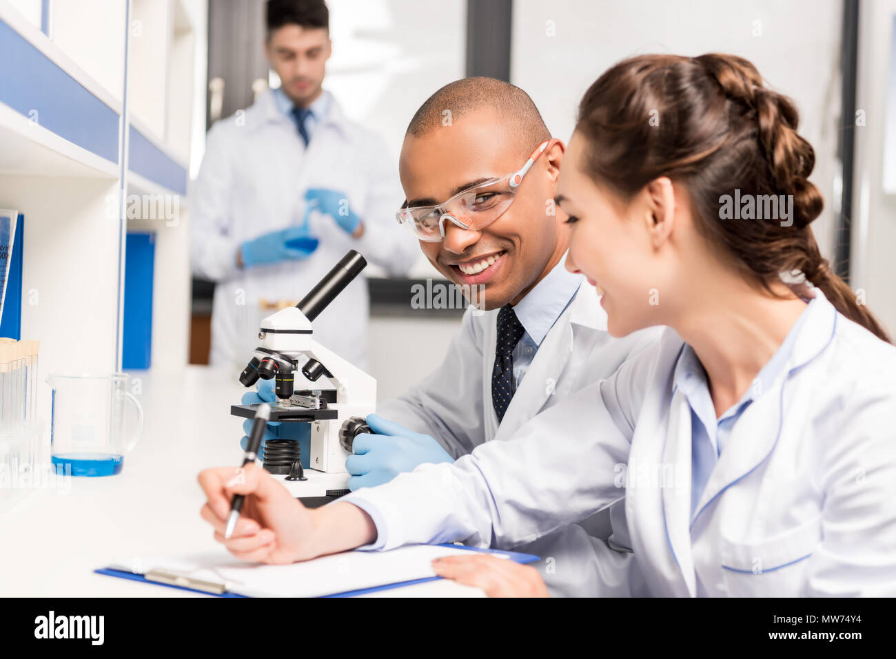 side view of smiling scientists working in laboratory with microscope ...