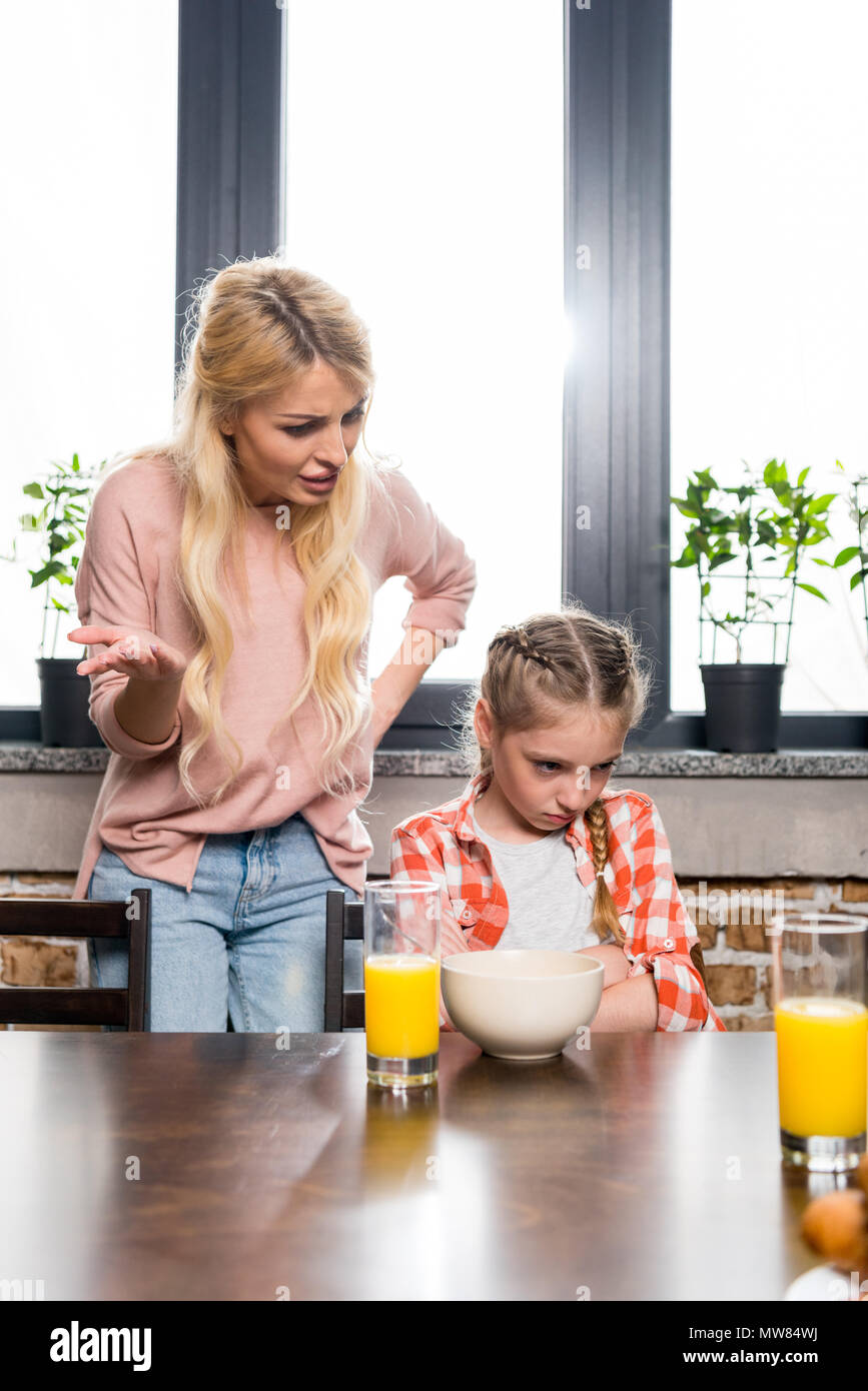irritated mother talking with upset little daughter during breakfast ...
