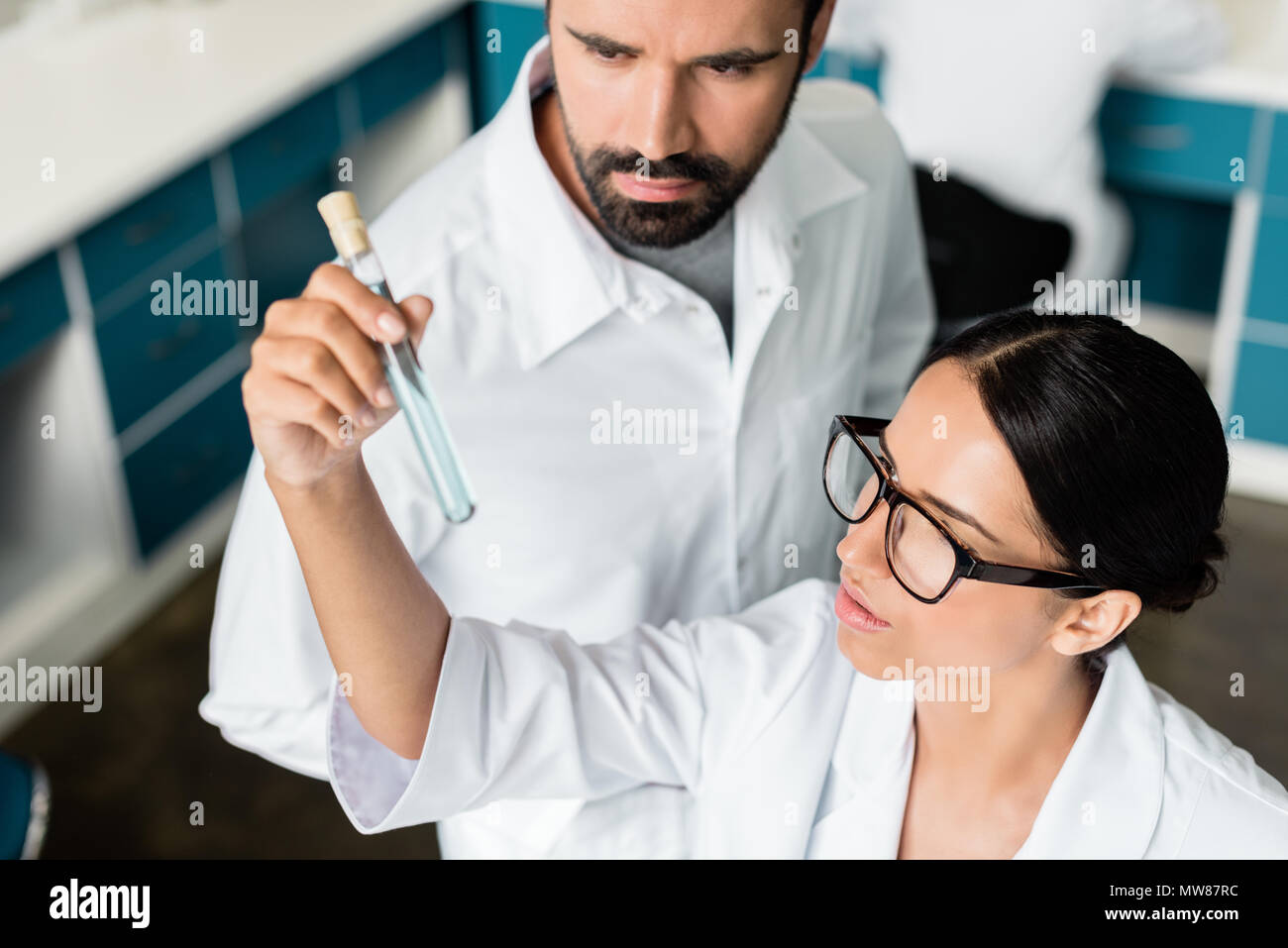 Professional young chemists in white coats examining test tube with ...