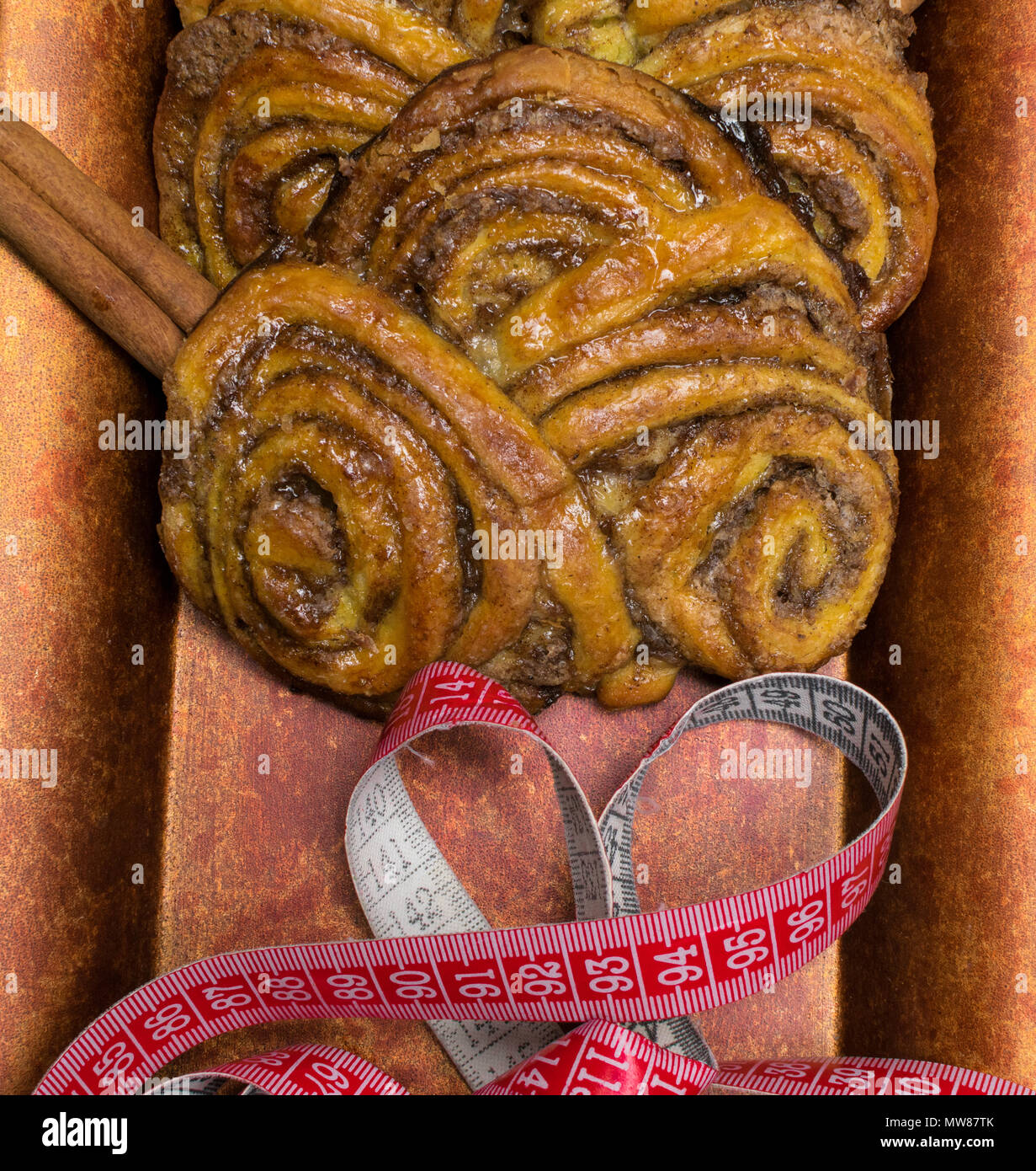homemade sweet cinnamon rolls on red plate with sticks of cinnamons and ...