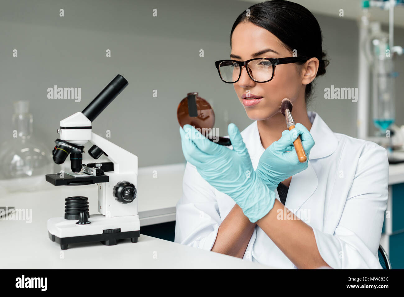 Attractive female scientist in eyeglasses applying makeup while working ...