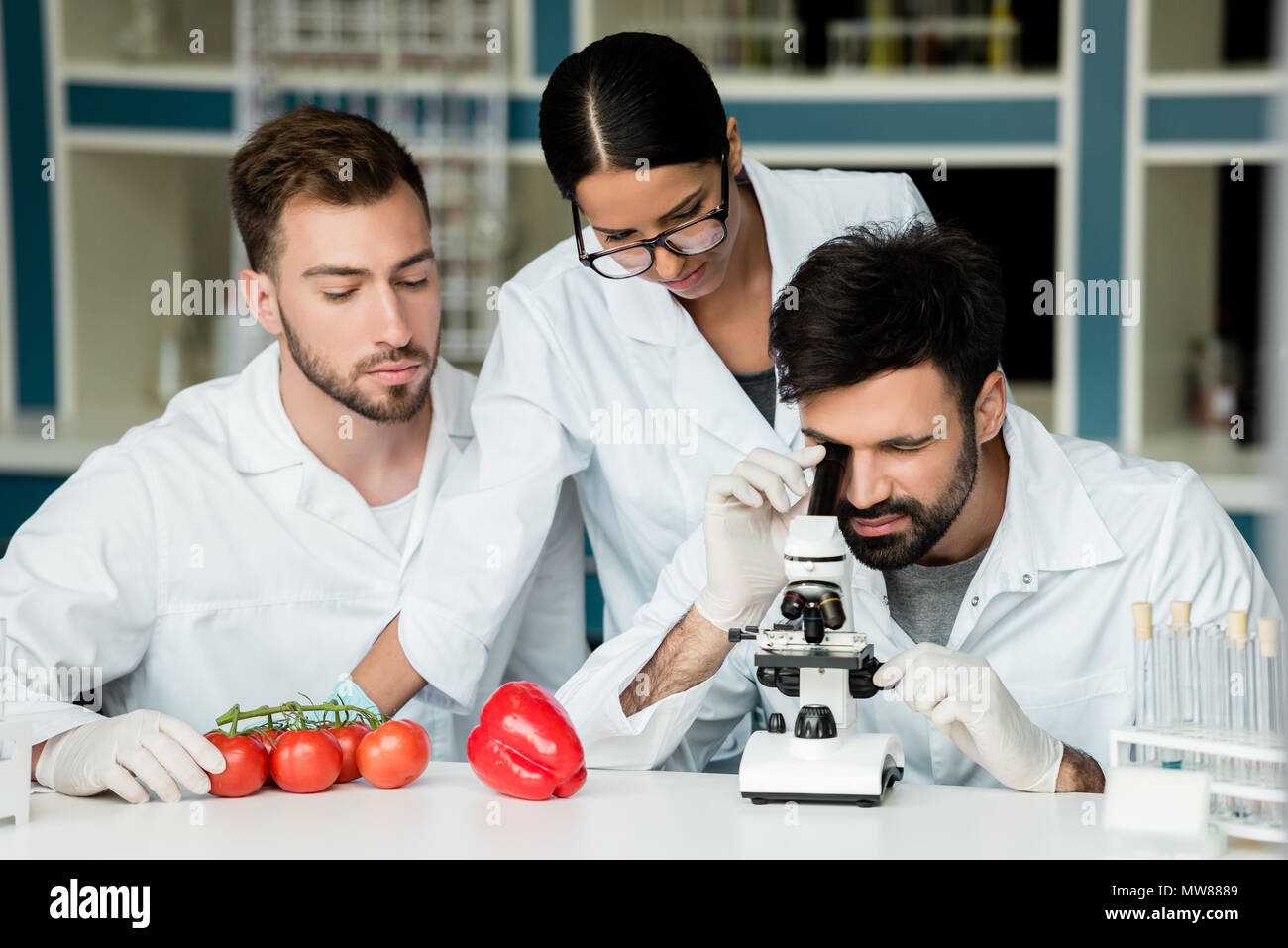 Professional young scientists in white coats using microscope while ...