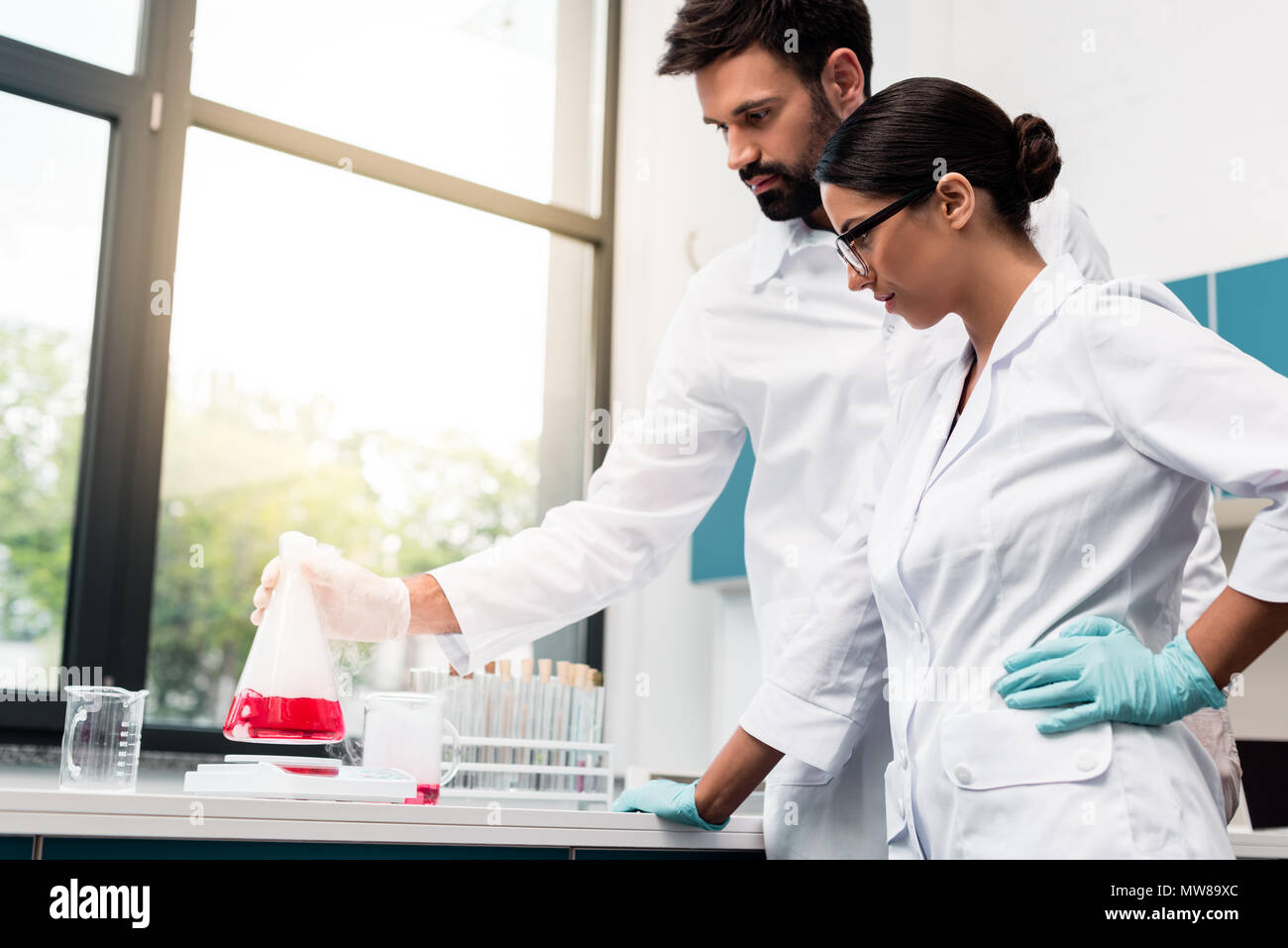 Focused young chemists in white coats making experiment while working ...