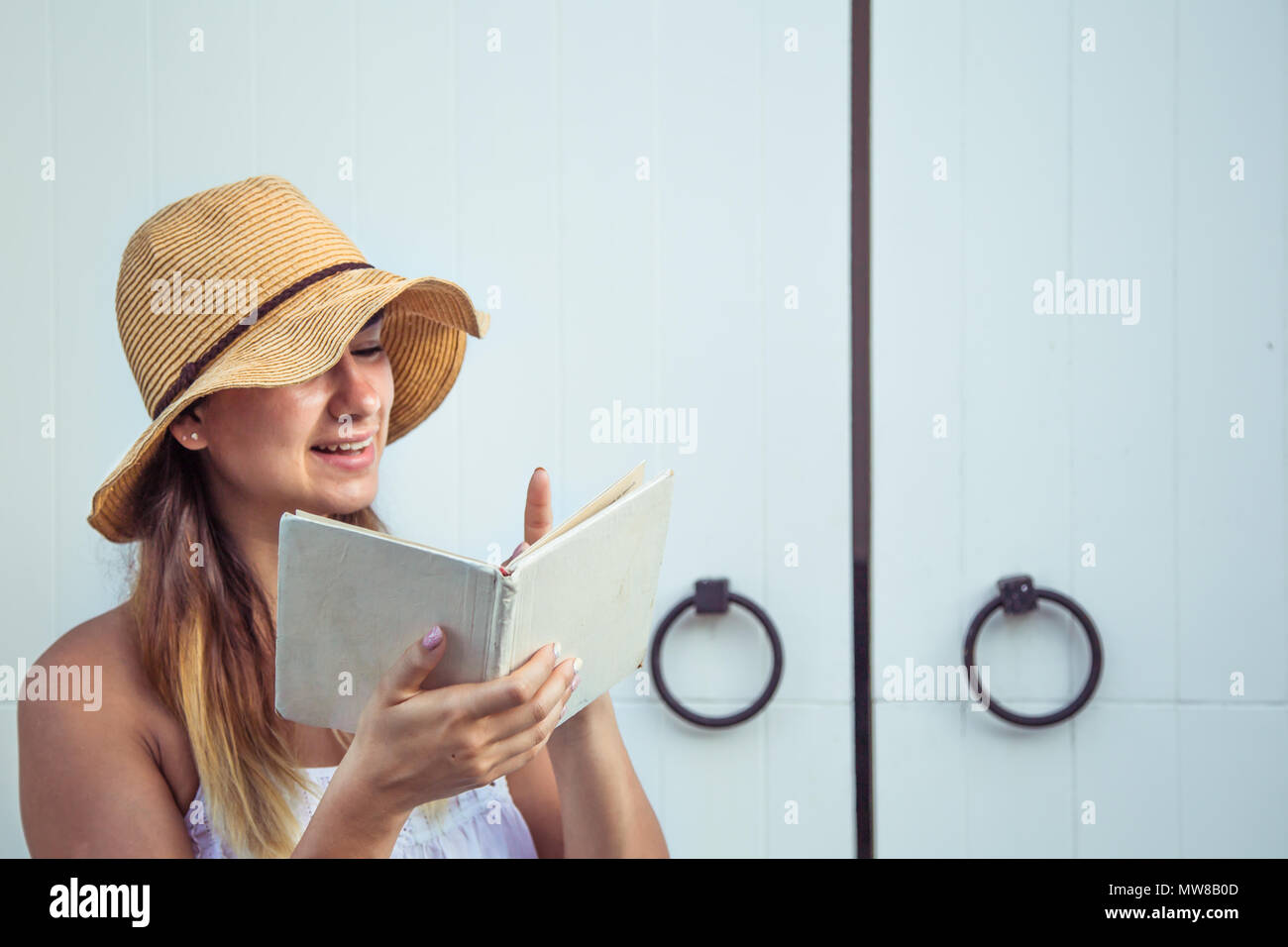 a young girl in a hat reading a book in a large white door, the concept ...