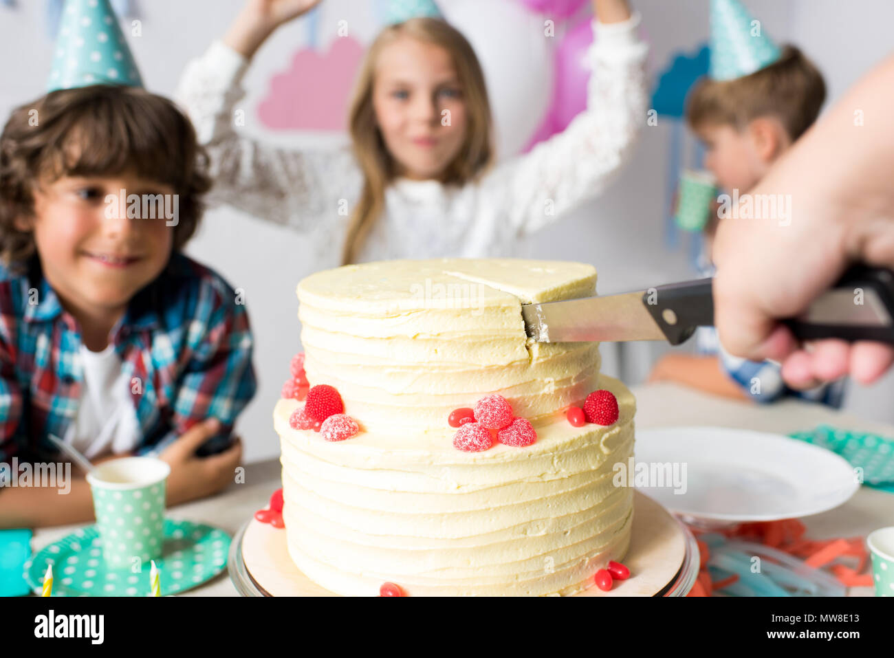 close-up view of hand cutting birthday cake and happy kids standing ...