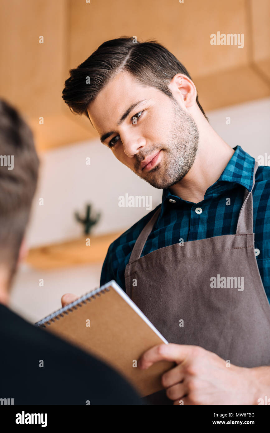 portrait of focused waiter in apron taking order from client in coffee ...
