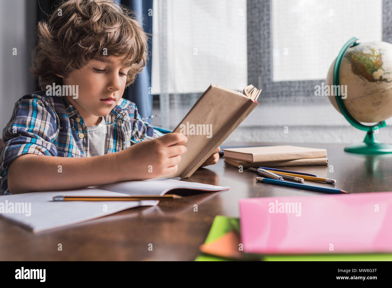concentrated little boy reading book while doing homework alone Stock ...
