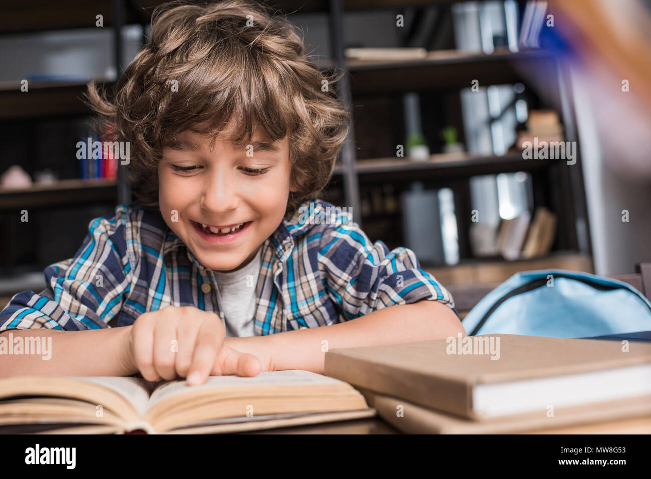 smiling little boy reading book while doing homework alone Stock Photo ...
