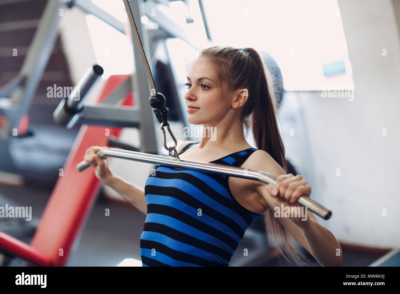 Young woman exercising pulling down lateral pull-down weights ...