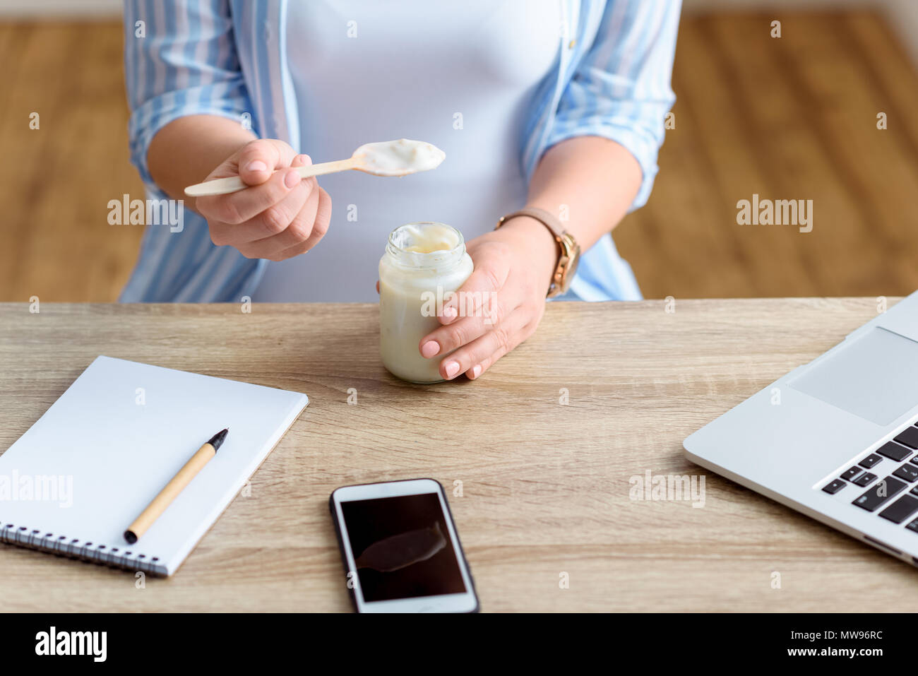 cropped view of pregnant woman eating yoghurt while sitting at table ...