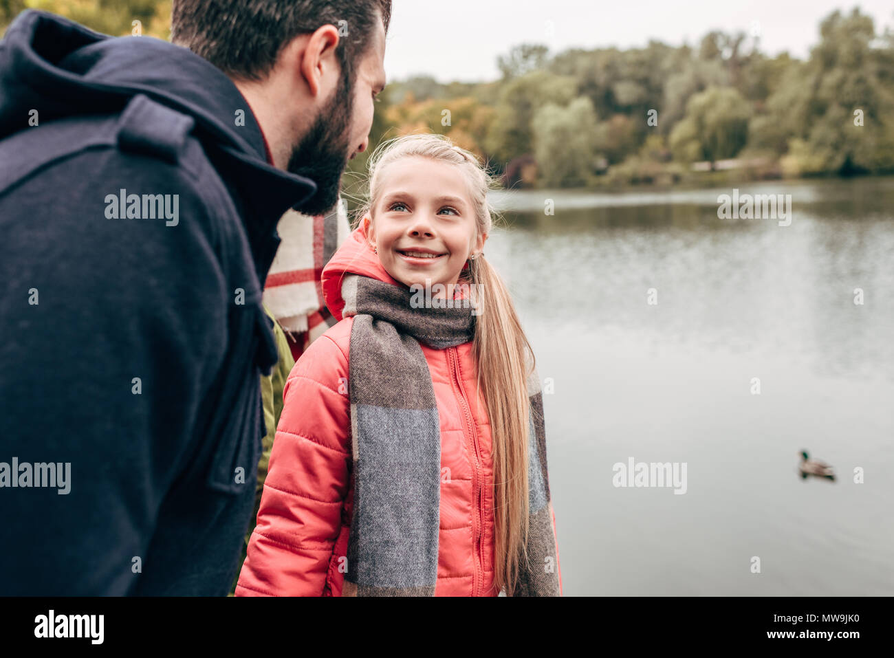 happy father and daughter smiling each other while standing near lake ...