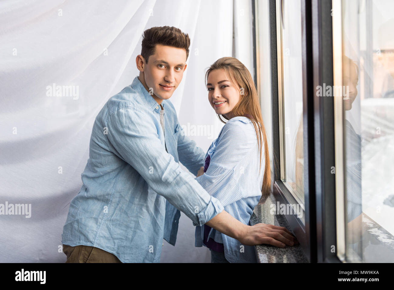 happy couple near window looking at camera Stock Photo - Alamy