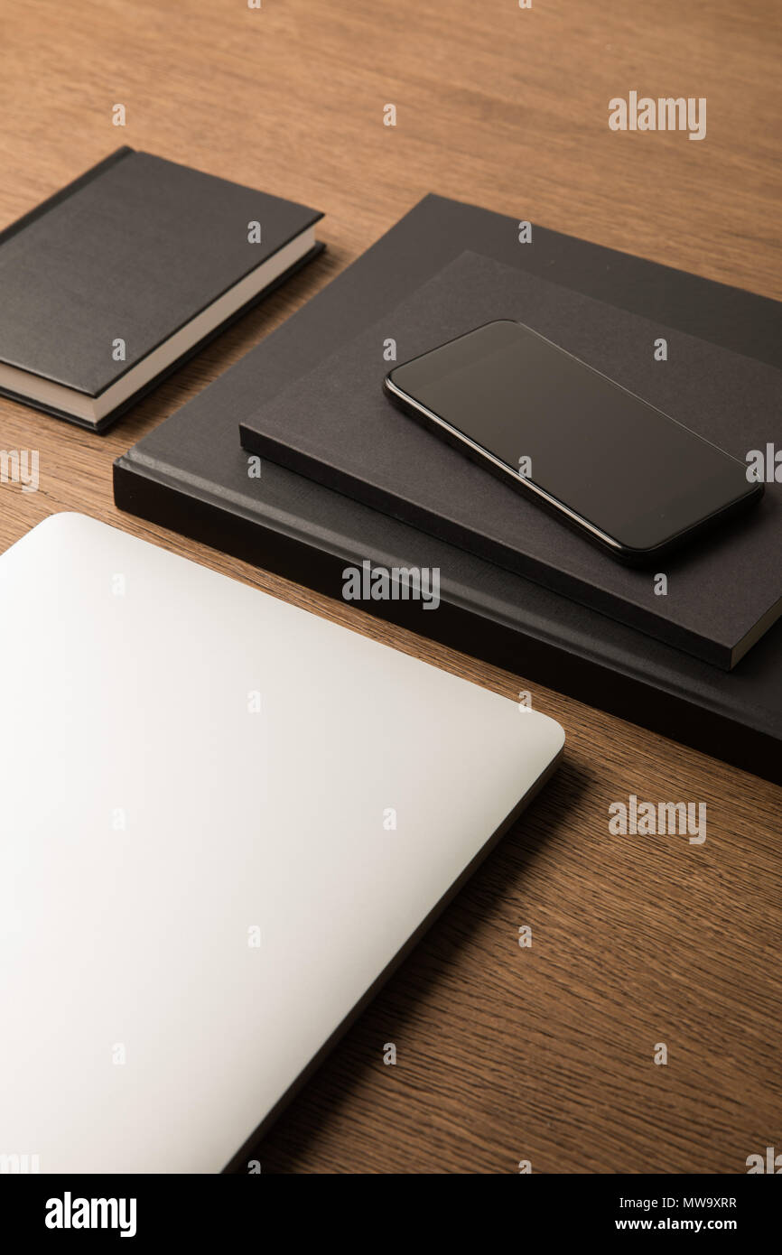 close up view of laptop, pile of black notebooks and smartphone on ...
