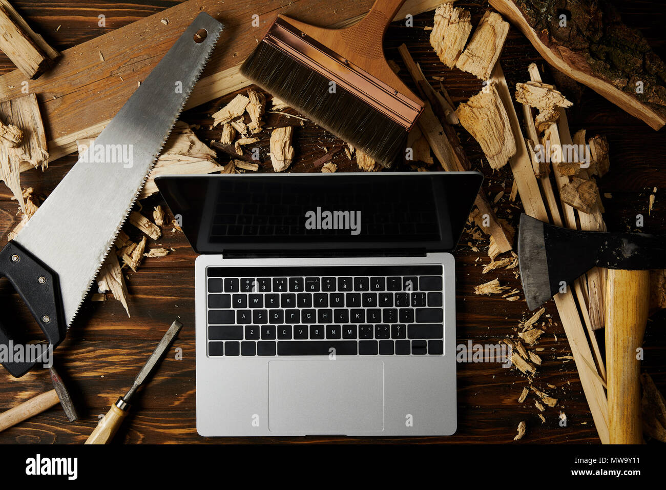 laptop with blank screen surrounded by axe, handsaw, chisel, paintbrush ...