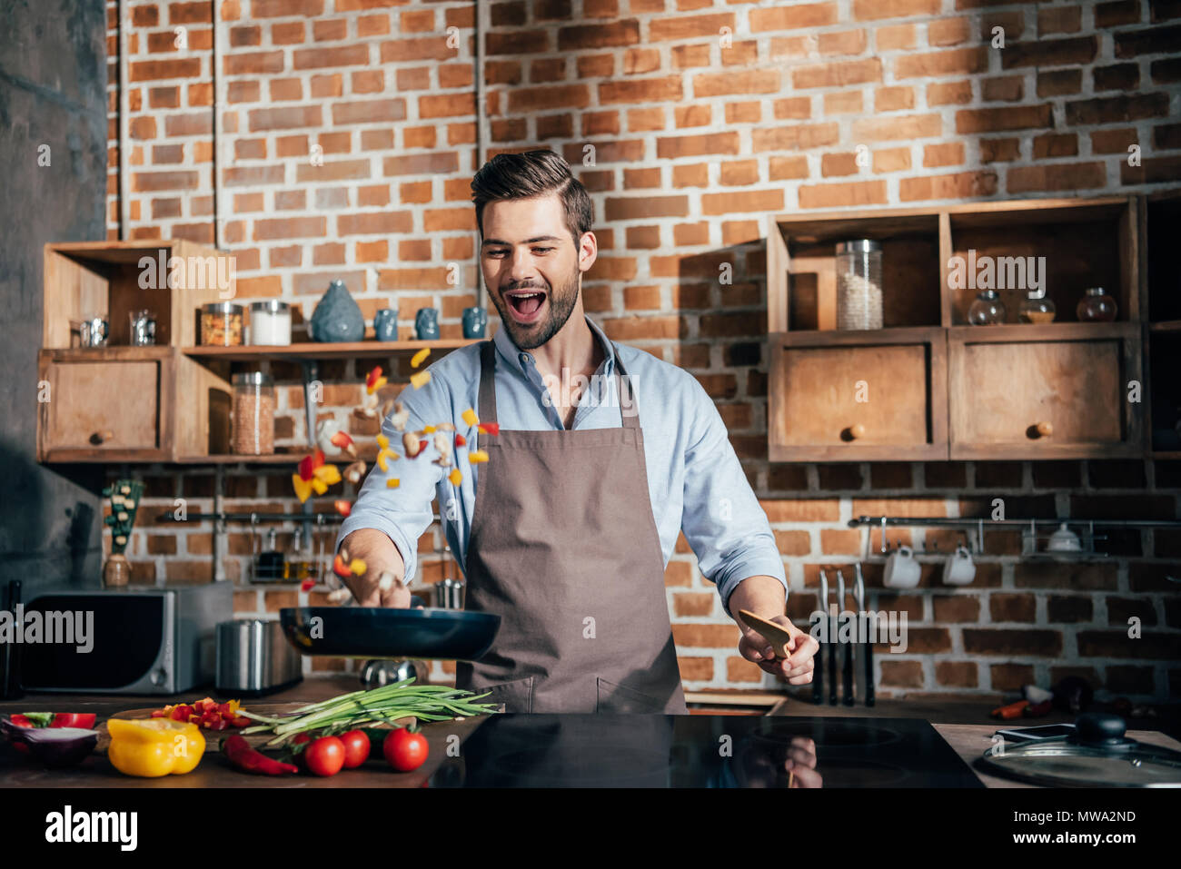 stylish young man with apron frying vegetables Stock Photo - Alamy