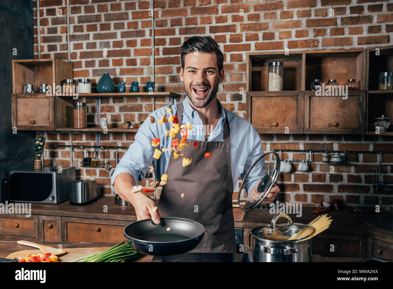 handsome young man with apron frying vegetables for pasta Stock Photo ...
