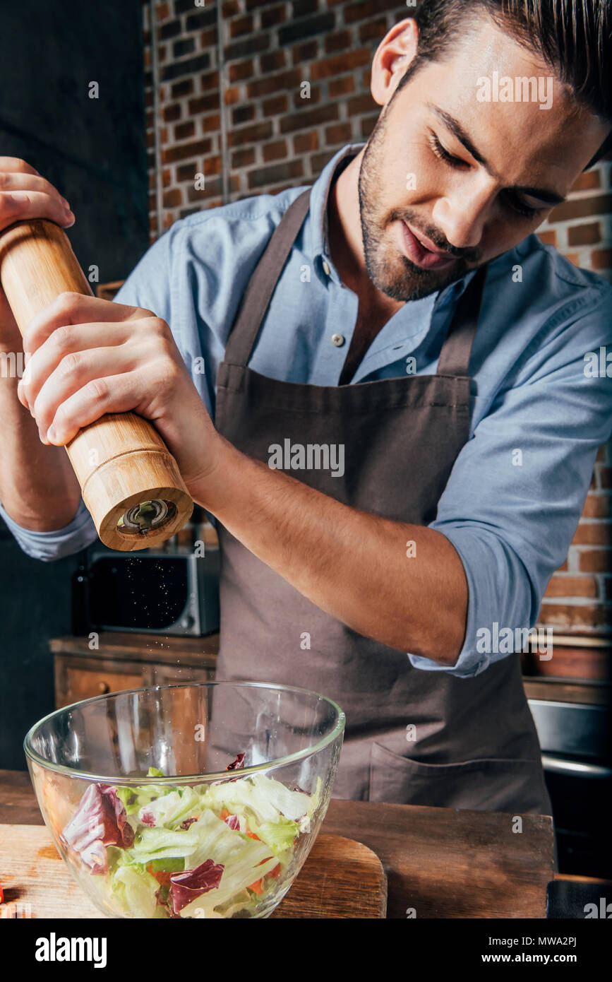 handsome young man adding pepper with mill into salad Stock Photo - Alamy