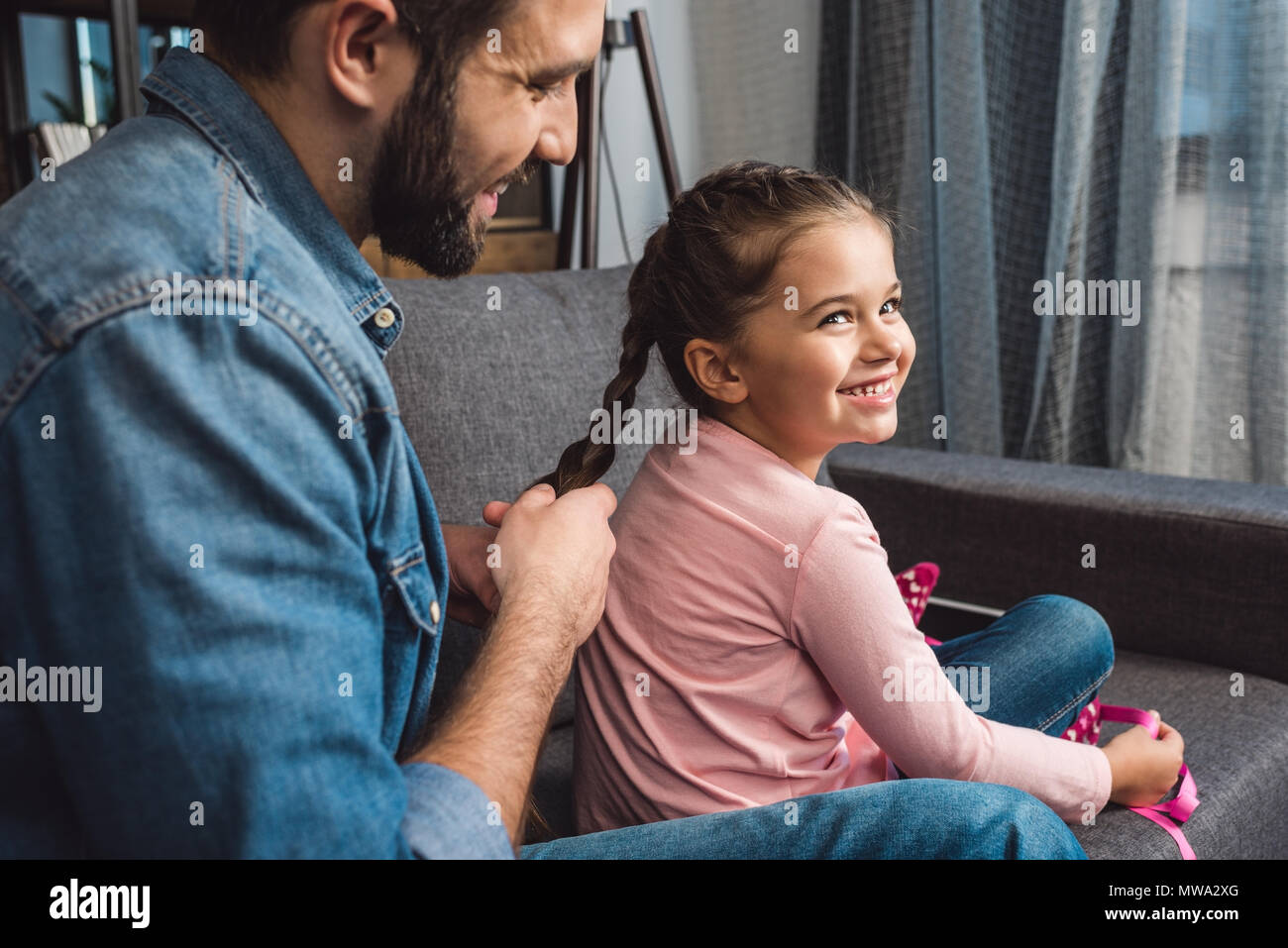 happy father making hair braid for daughter while sitting on couch at ...