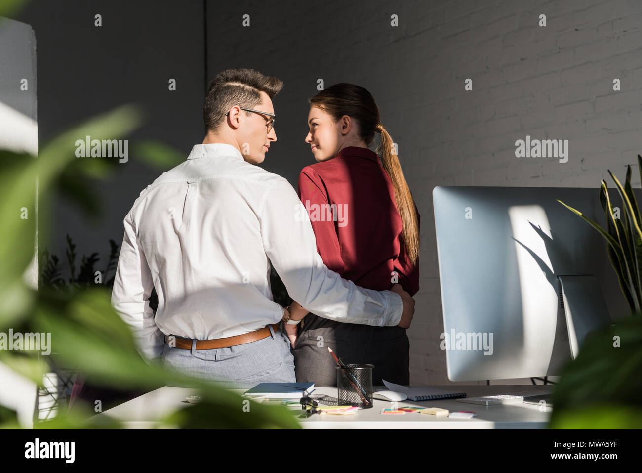 rear view of managers embracing at workplace, office romance concept ...