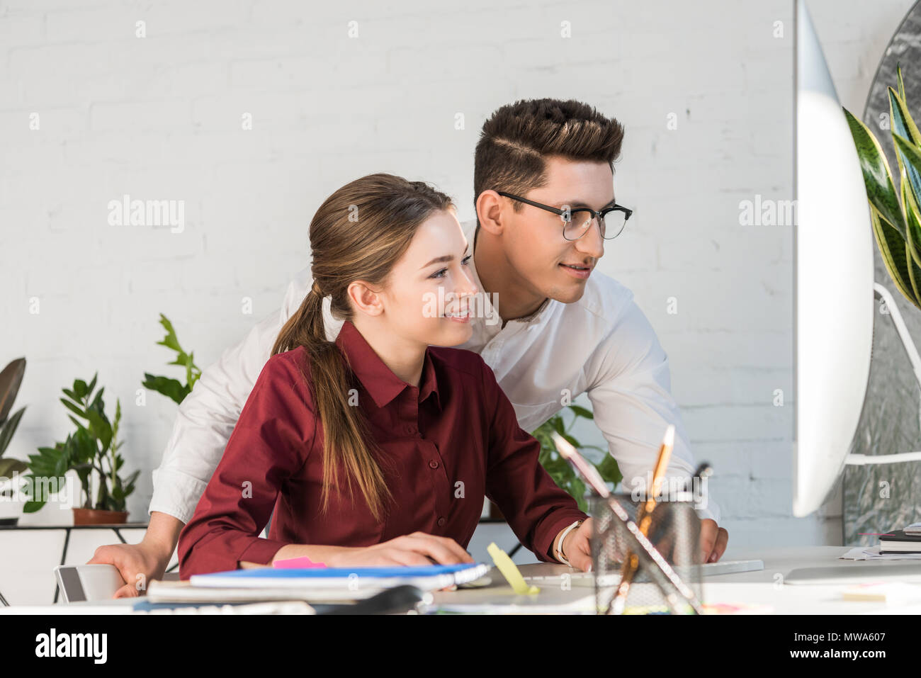 businessman helping his colleague with computer work and embracin her ...