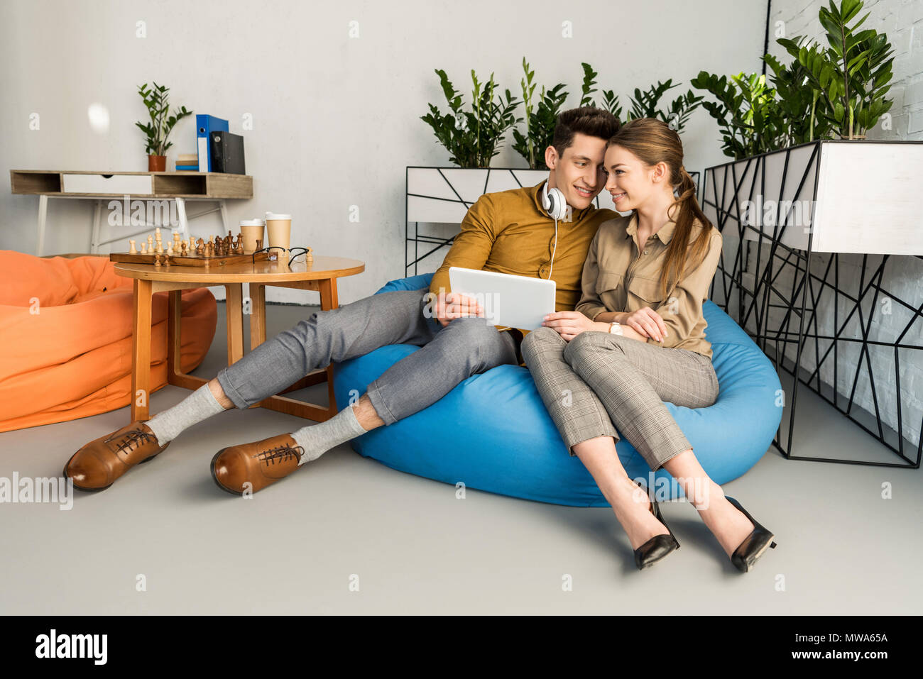 young couple cuddling using tablet together while sitting in bean bag ...