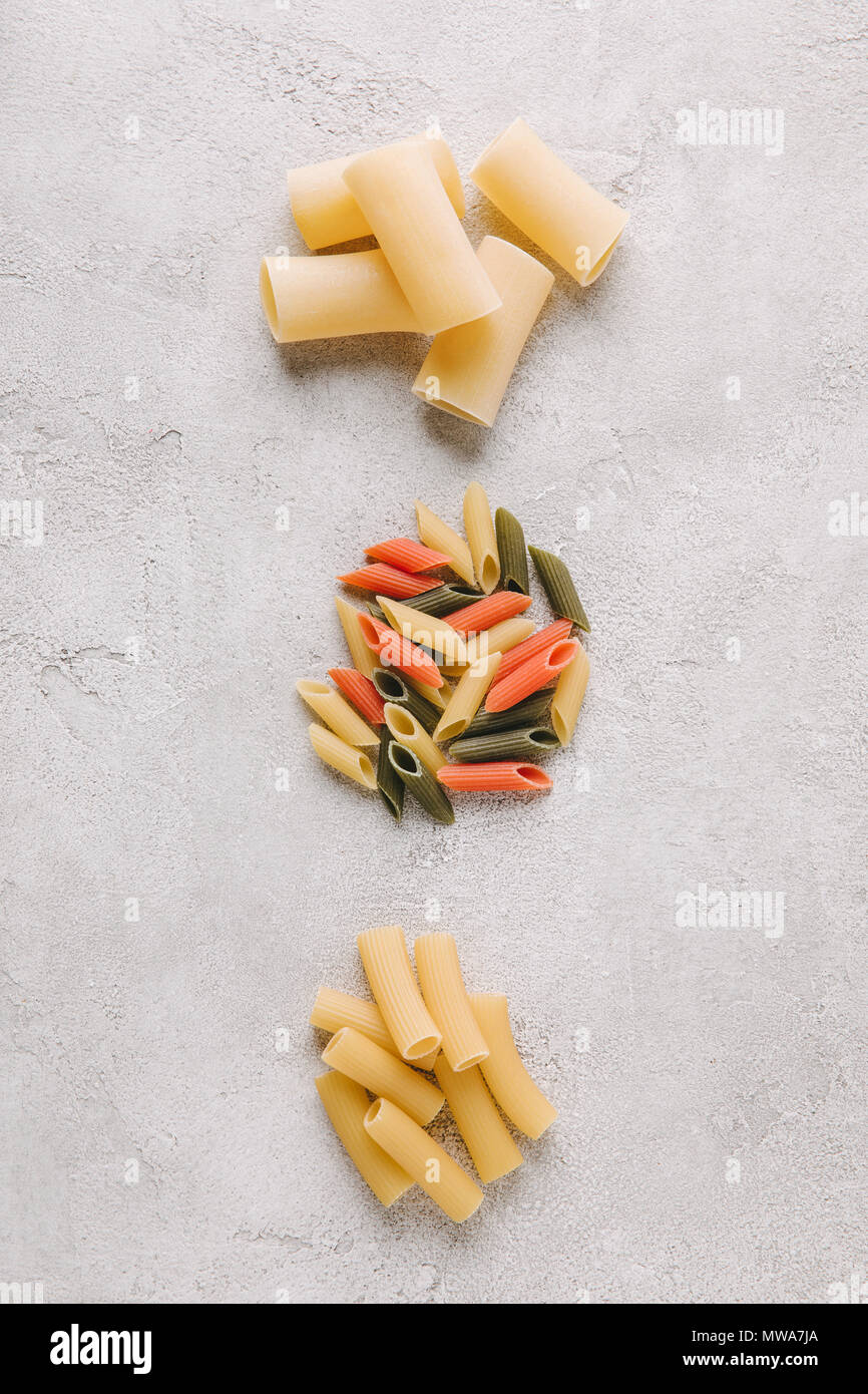 top view of piles of different raw pasta in row on concrete surface ...