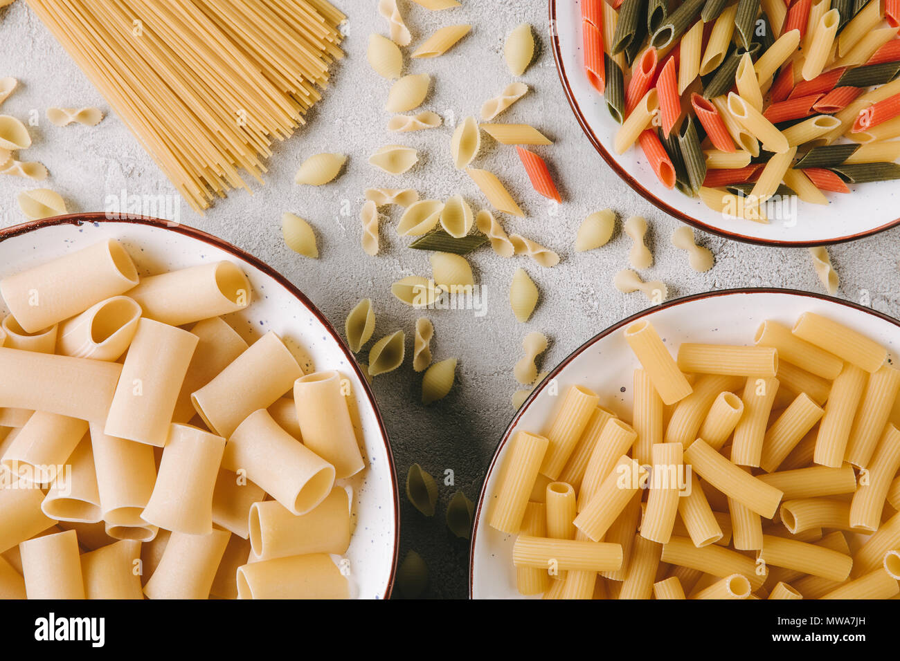 top view of different raw pasta in bowls on messy concrete surface ...