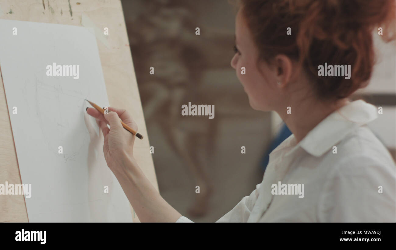 Young woman drawing in pencil using easel and explaining the process ...
