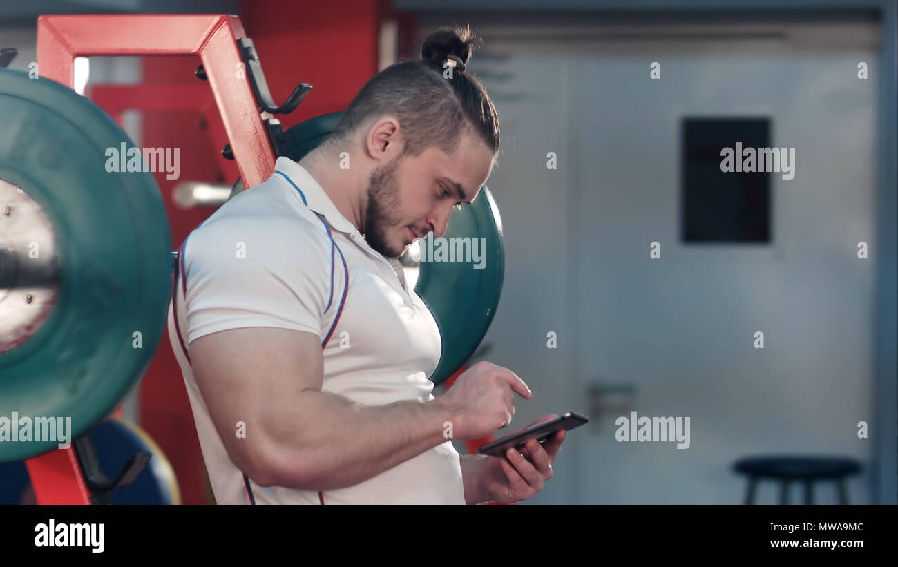 Bodybuilder using digital tablet to track his workout progress in gym ...