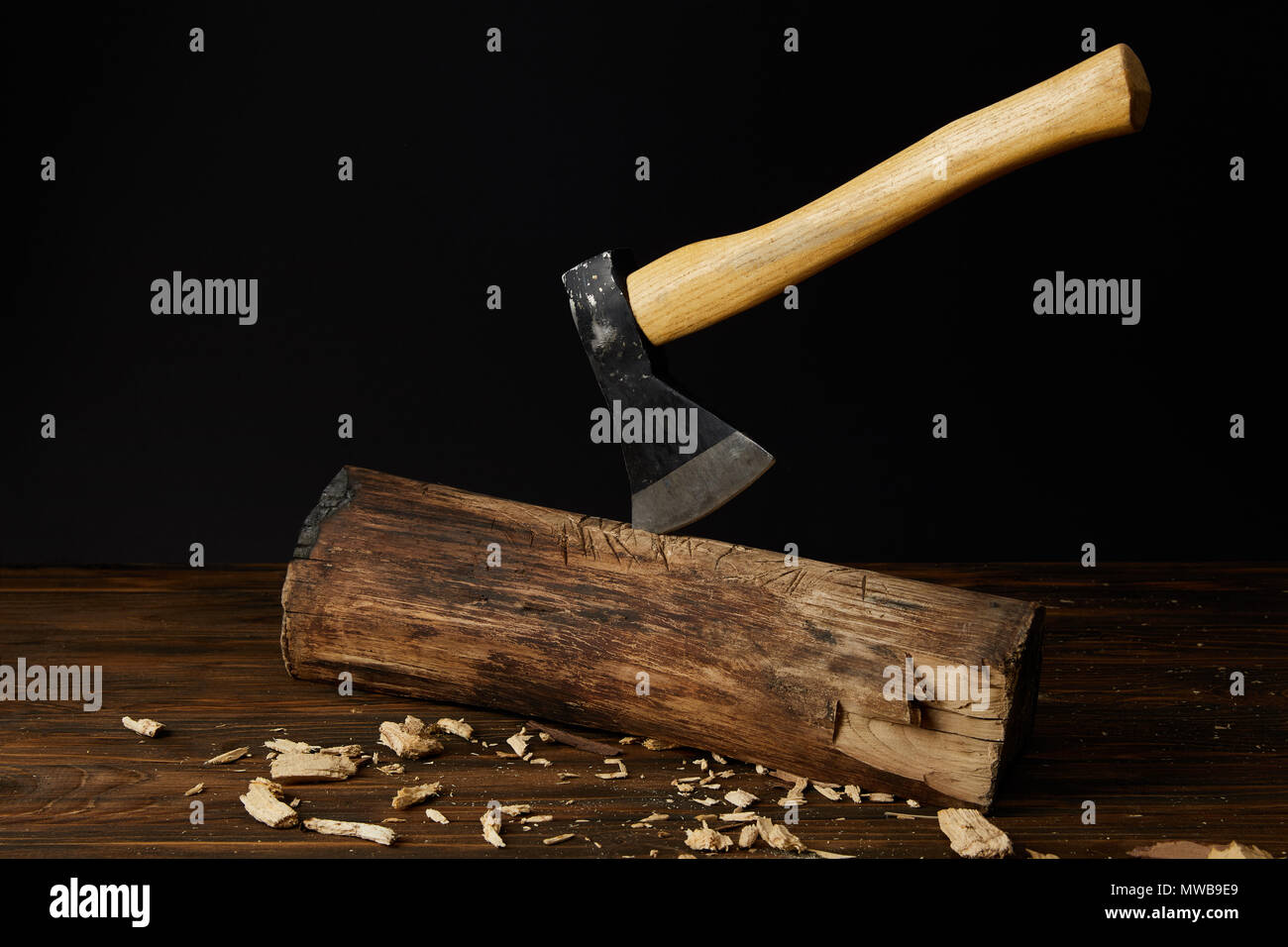log with sticking axe and wooden pieces at table on black background ...