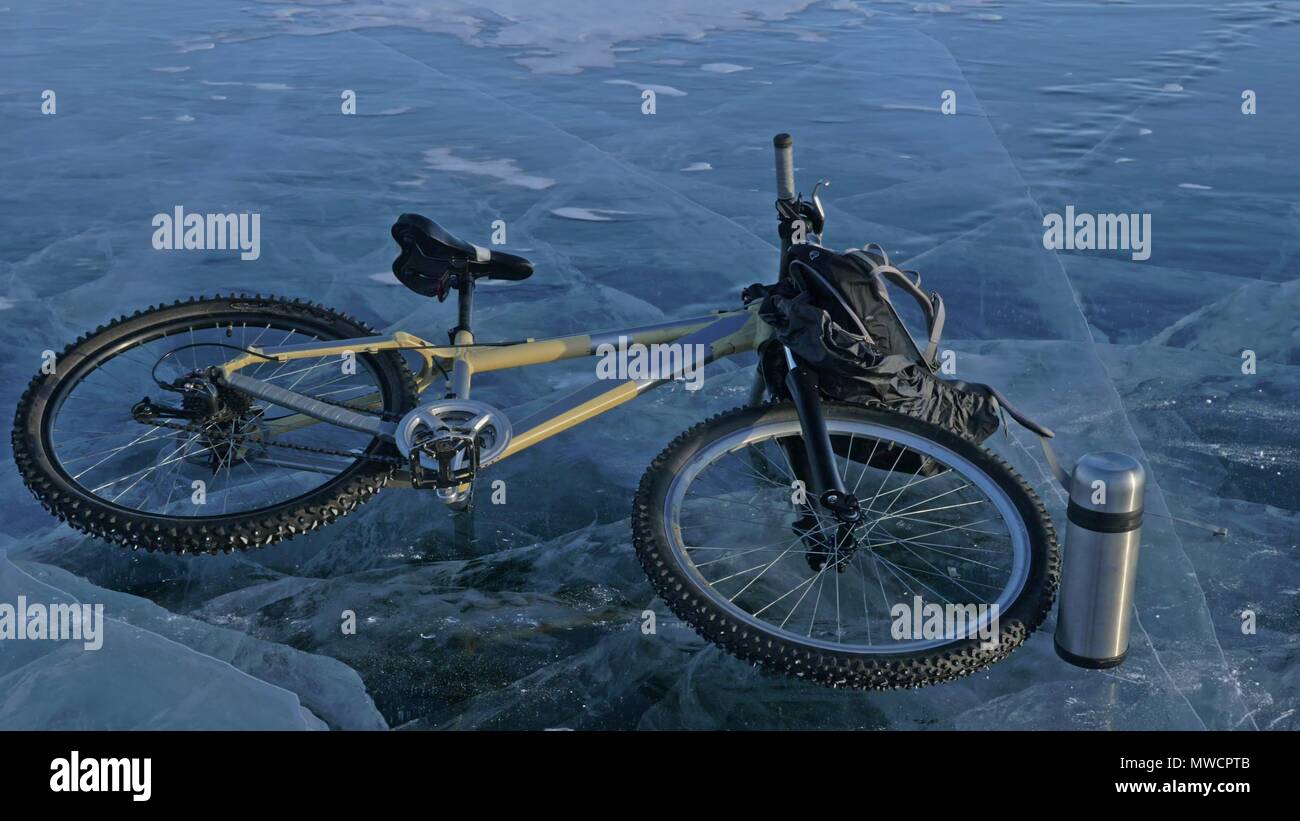 Man and his bicycle on ice. He looks at the beautiful ice in the cracks ...