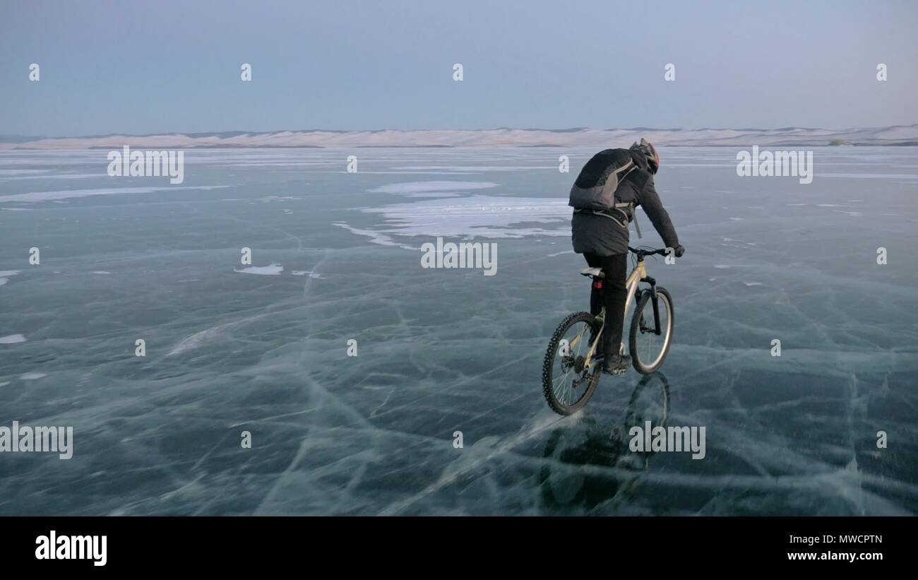 Man is riding a bicycle on ice. The cyclist is dressed in a gray down ...