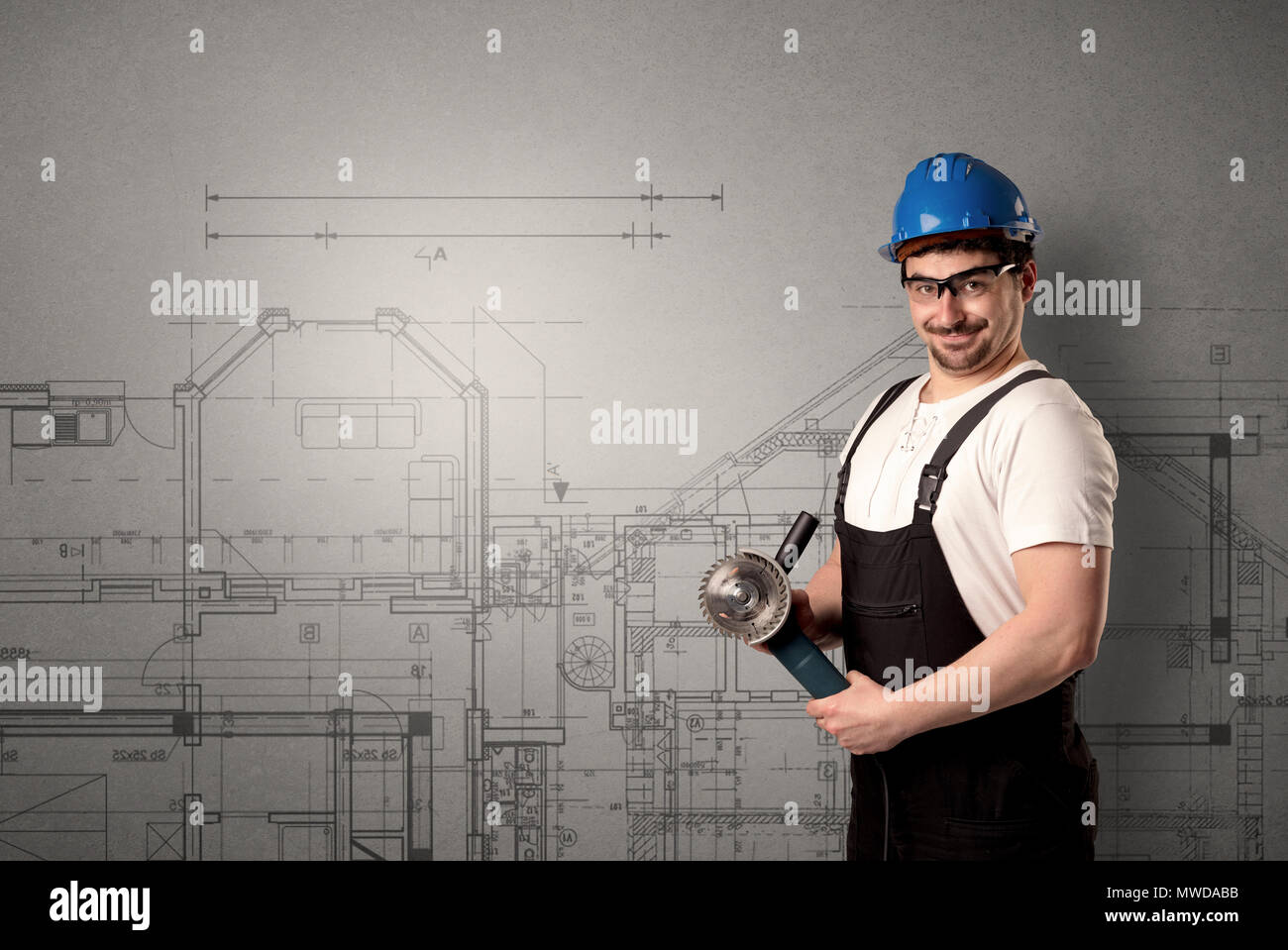 Worker standing with tool in his hand in front of technical drawings ...