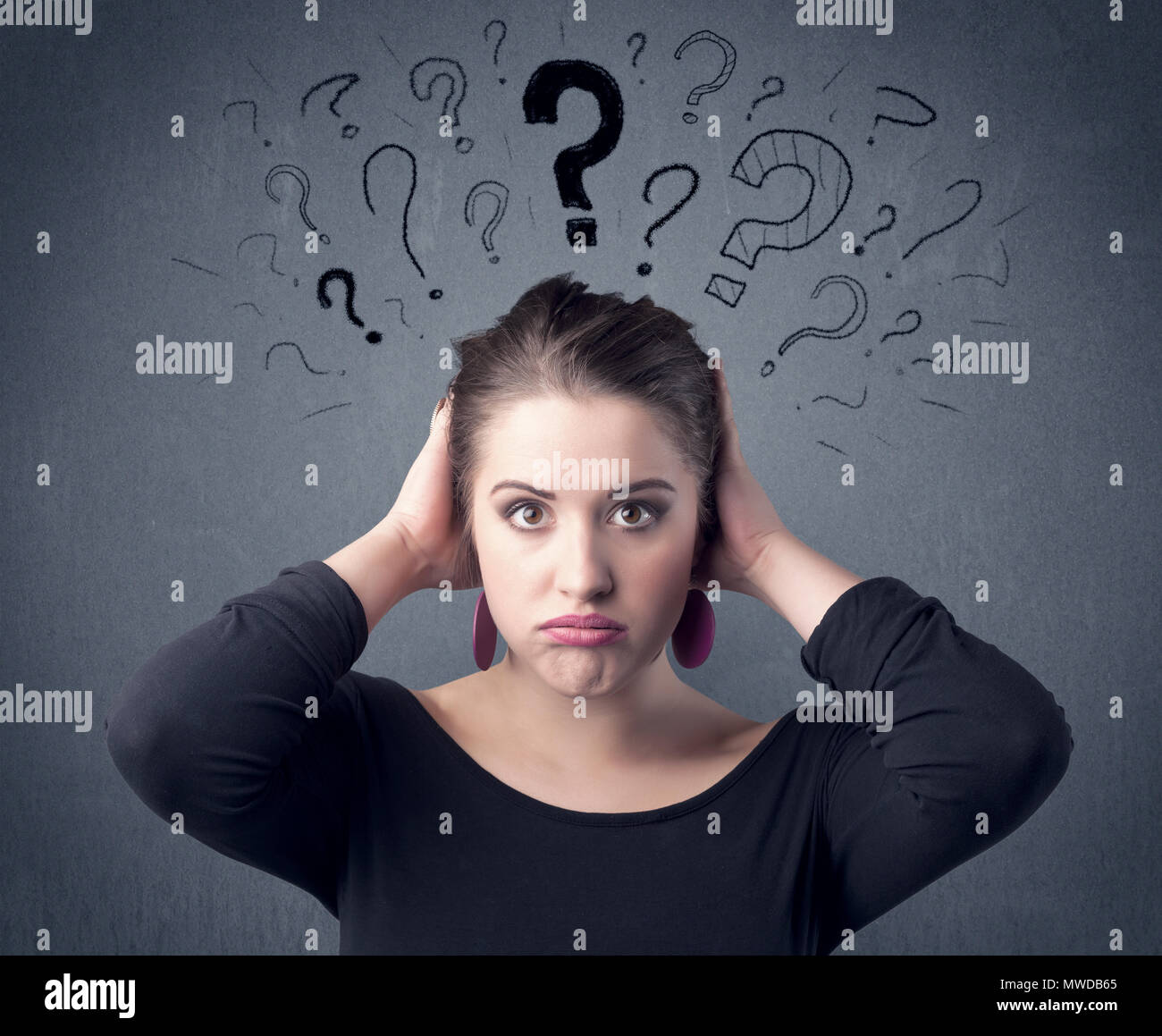 A pretty teenage girl standing confused in front of grey wall ...
