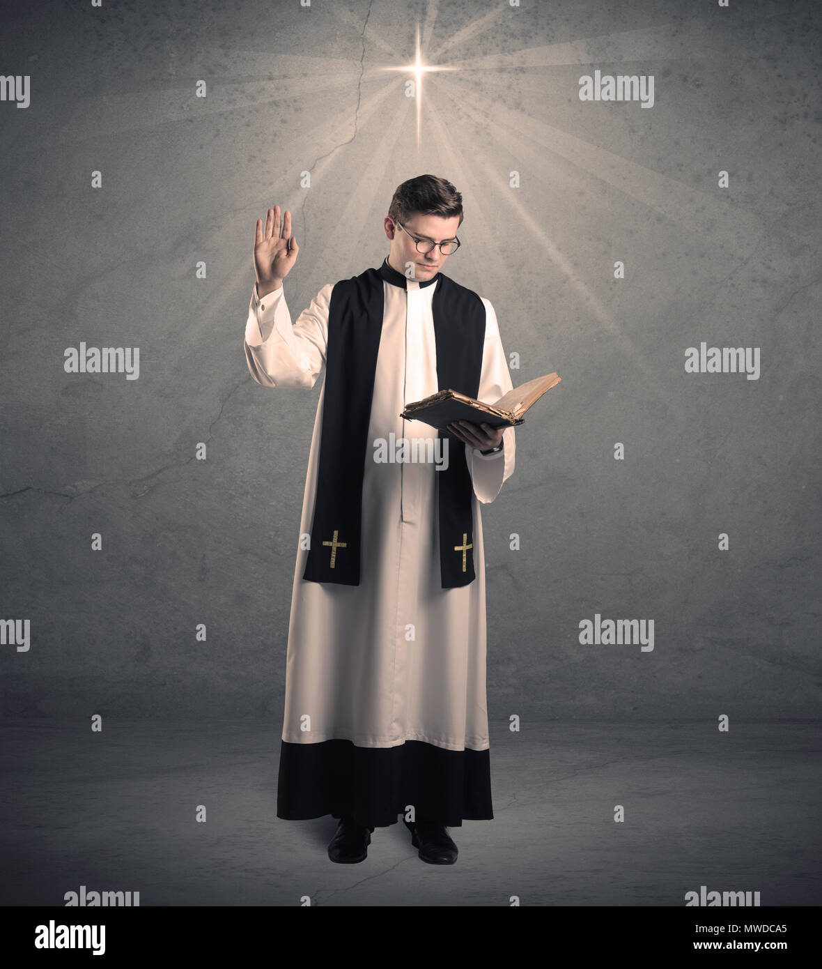 A young male priest in black and white giving his blessing in front of ...