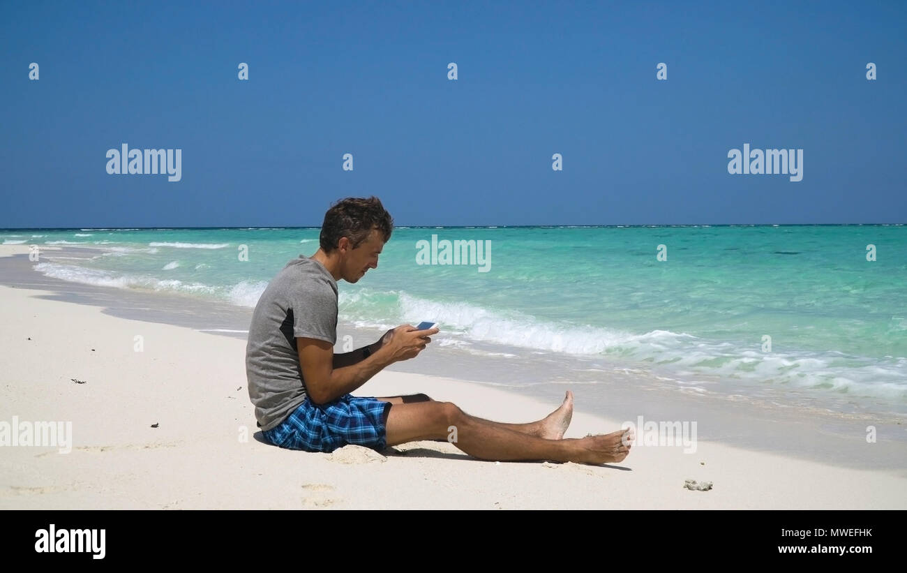 Man using electronic tablet on the beach. Man sits on a sandy beach and ...