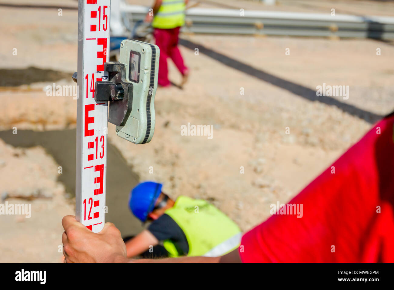 Construction worker is holding leveling rod to help surveyor, geodesist ...