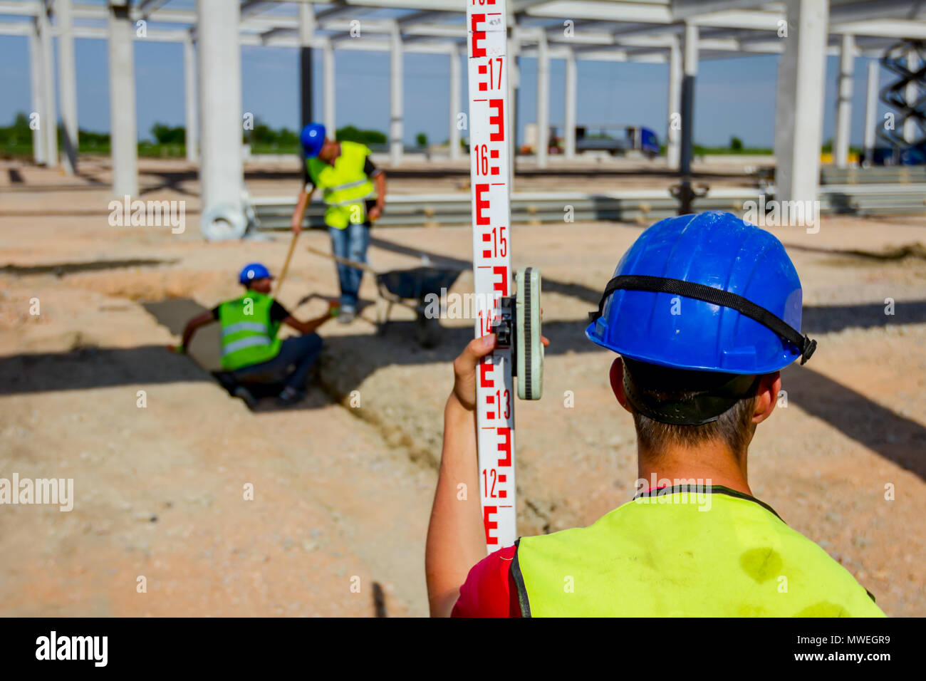 Construction worker is holding leveling rod to help surveyor, geodesist ...