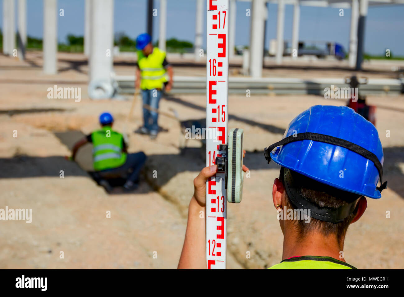 Construction worker is holding leveling rod to help surveyor, geodesist ...