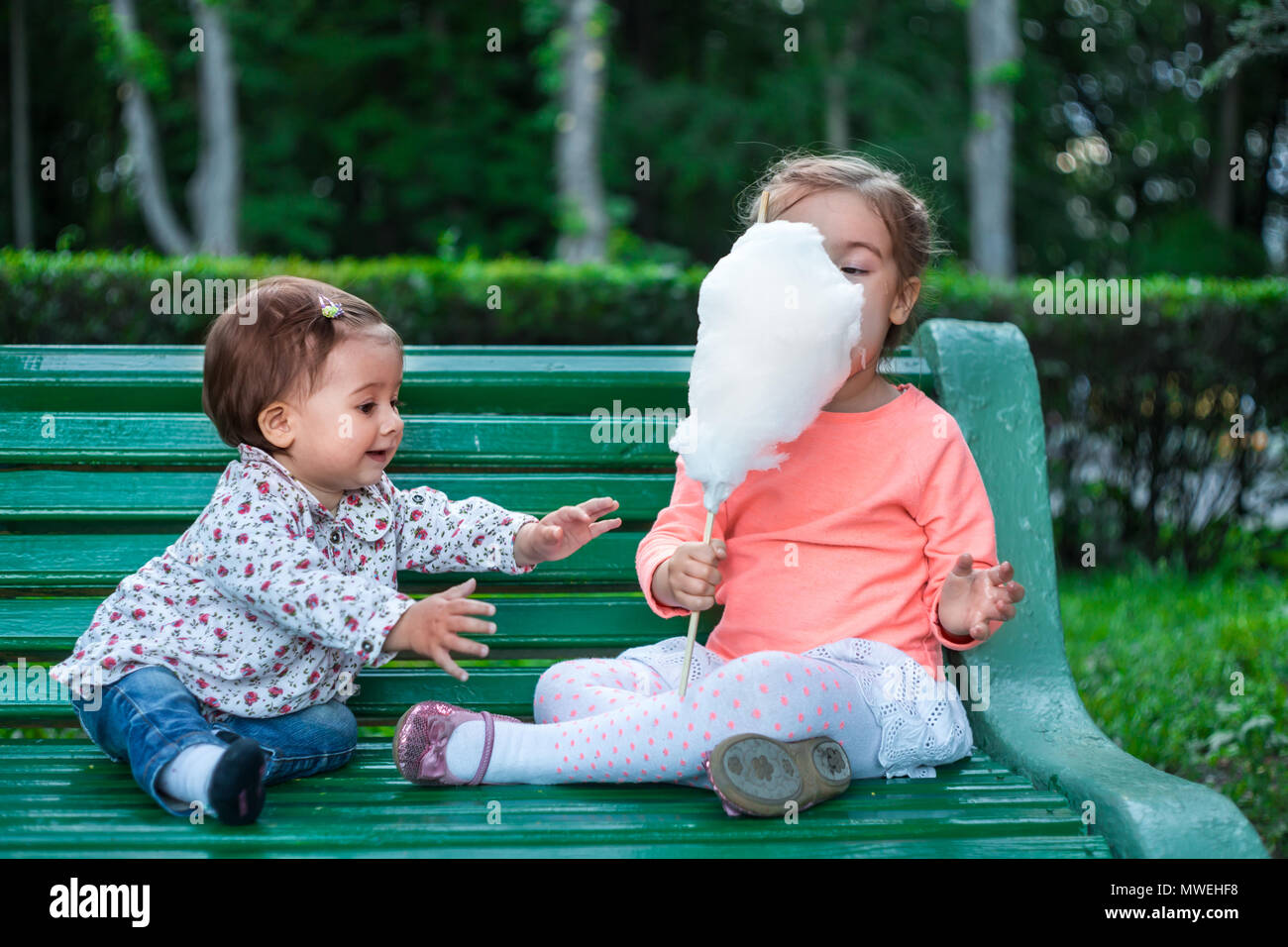 little girl eating cotton candy while sitting on a Park bench Stock ...