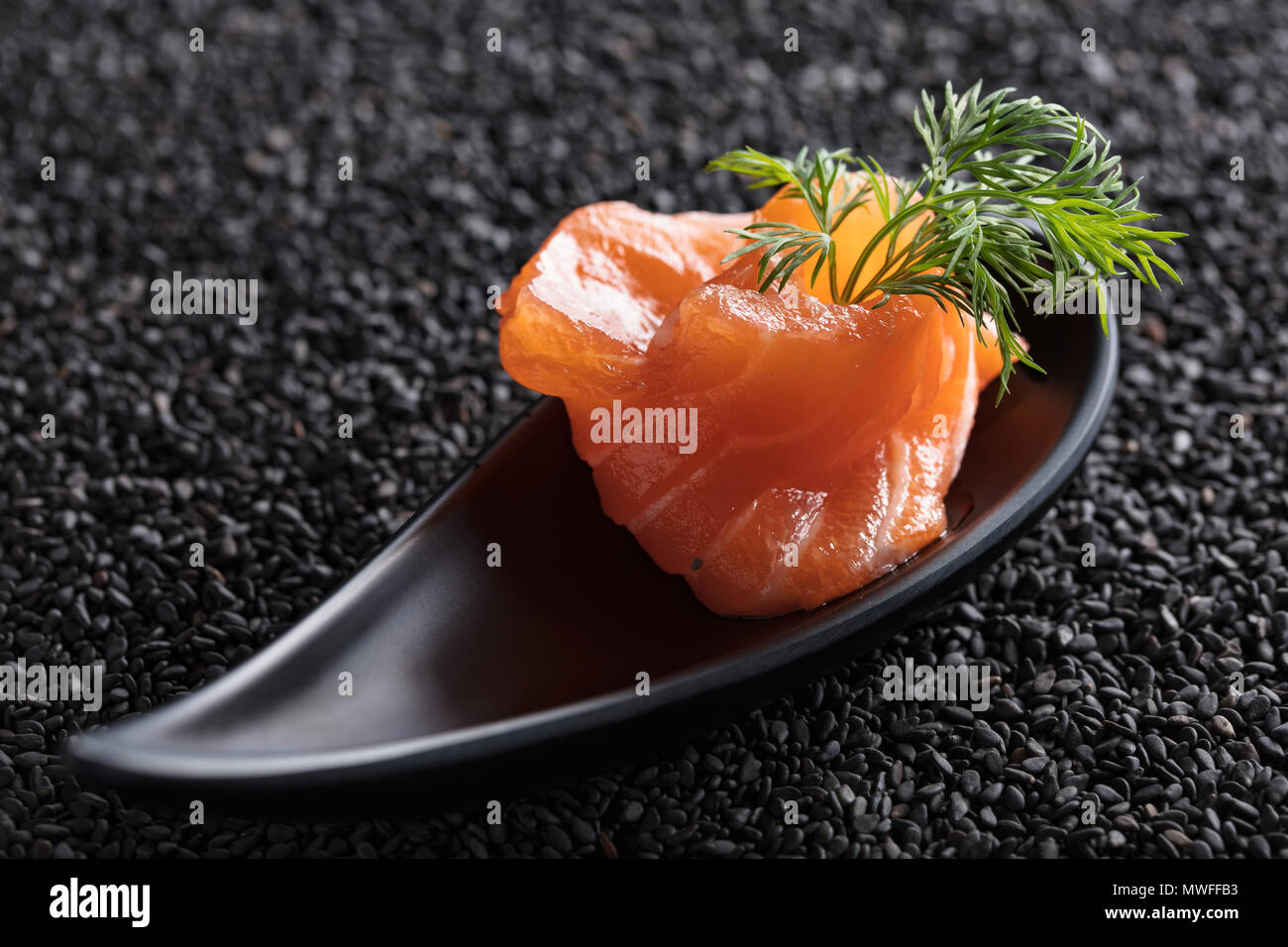 Slice of salted salmon with dill on the background of black sesame ...