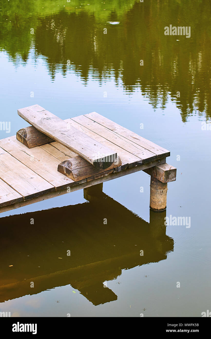 Cozy fishing bench on a wooden pier at the shore of a calm pond or lake ...