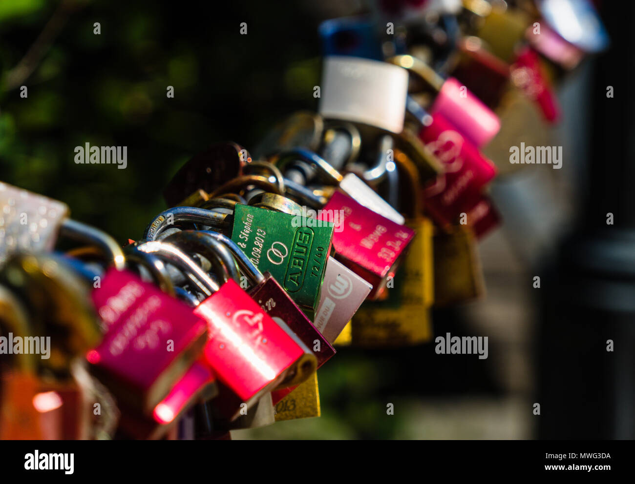 Locked padlocks with engraved names on the chain of a bridge railing as ...