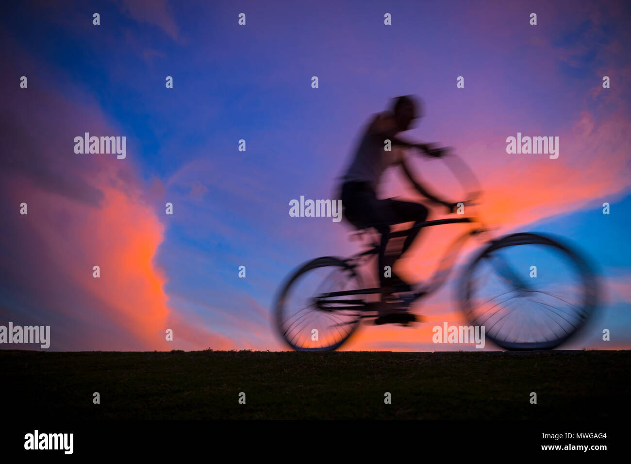 Colorful sunset view of a silhouette of a man riding a bike with motion ...