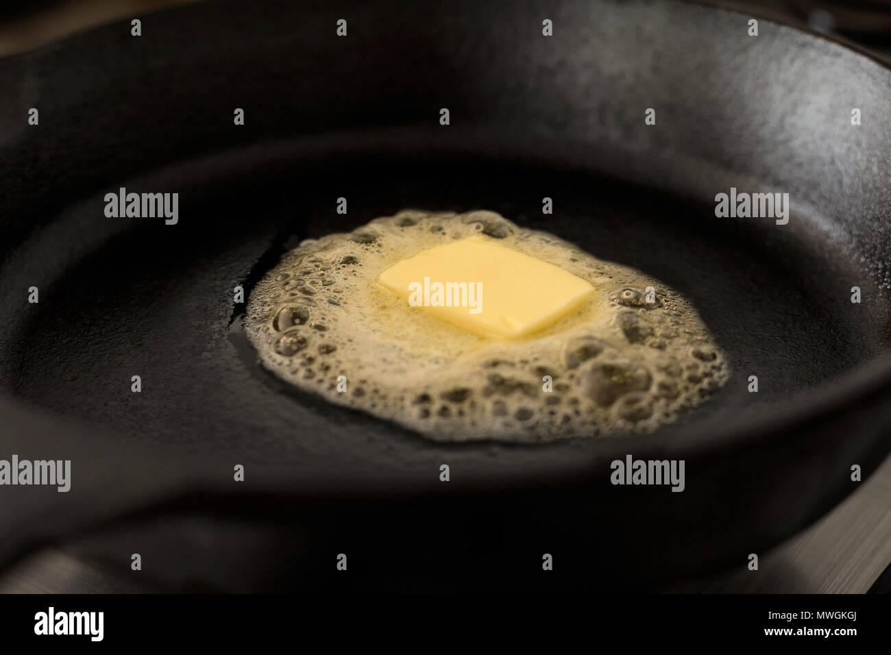 A butter pat melting on a black cast iron frying pan Stock Photo - Alamy