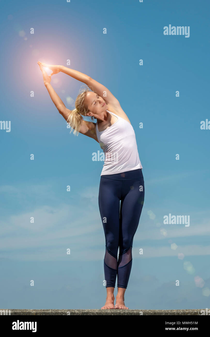 woman standing practicing yoga outside with a blue sky background with ...