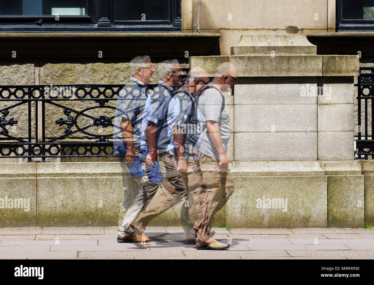 Multiple exposure image of two men walking past a sandstone building ...